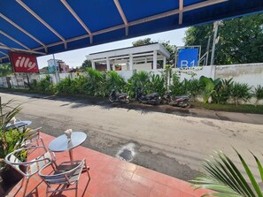 Uma área de estar coberta ao ar livre com cadeiras e mesas de metal, um edifício com uma placa azul e motocicletas estacionadas.
