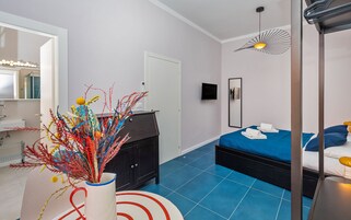 Quarto de hotel moderno com cama, cómoda, espelho e um vaso com ramos coloridos.