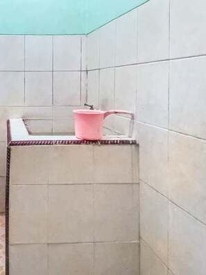 Uma casa de banho pequena com azulejos brancos, uma bacia rosa e chão em mosaico.