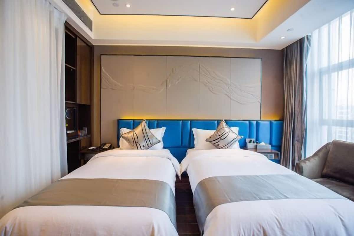 Quarto de hotel com duas camas, uma obra de arte grande fixada na parede e vista para a cidade.
