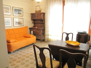 Uma sala de estar com sofá, mesa de madeira, cadeiras, um pequeno armário e quadros nas paredes.