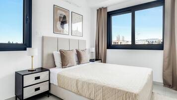 Um quarto moderno com uma cama grande, uma mesa de cabeceira com abajur e duas fotos emolduradas na parede.