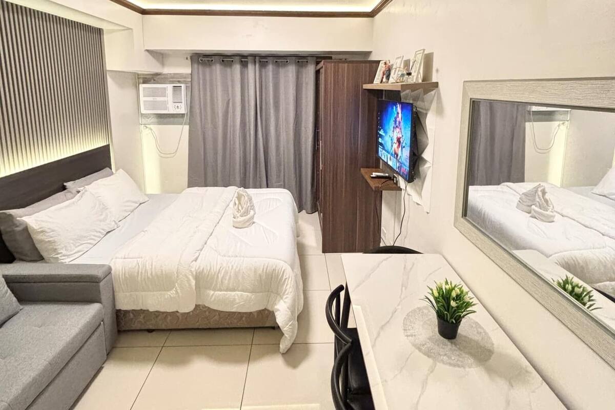 Quarto de hotel moderno com cama, televisão, escrivaninha e um espelho grande.