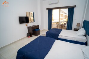Quarto de hotel com duas camas, televisão, escrivaninha e janela com cortinas.