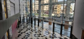 Um corredor com piso ladrilhado, janelas amplas e vista para o exterior.