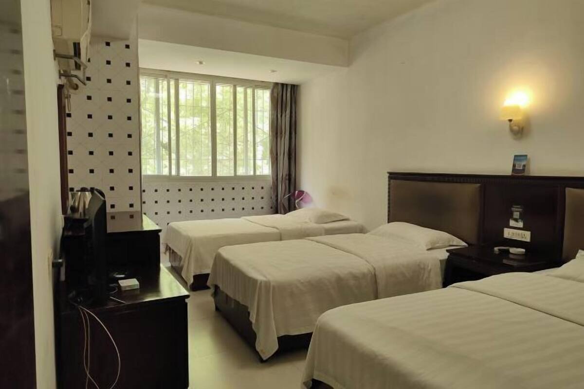 Quarto de hotel com duas camas, uma escrivaninha, uma televisão e uma janela com cortinas.