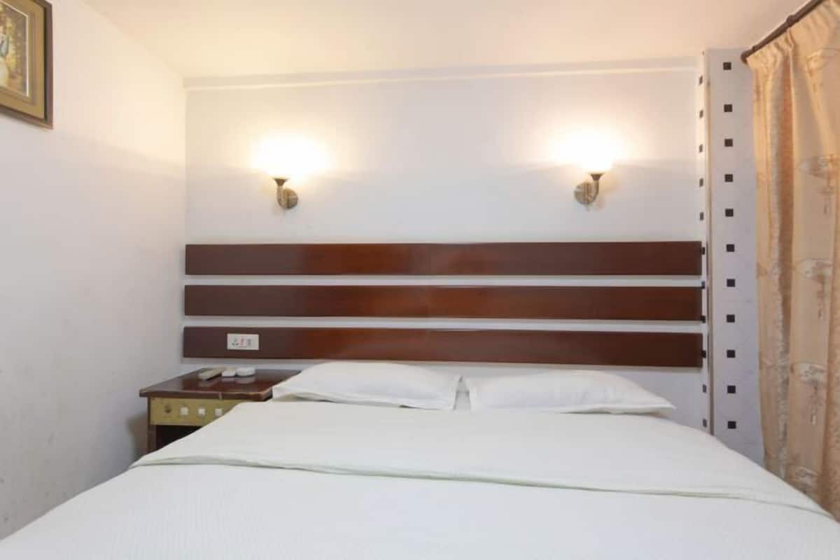 Quarto de hotel com uma cama, mesa de cabeceira e duas luzes fixadas na parede.