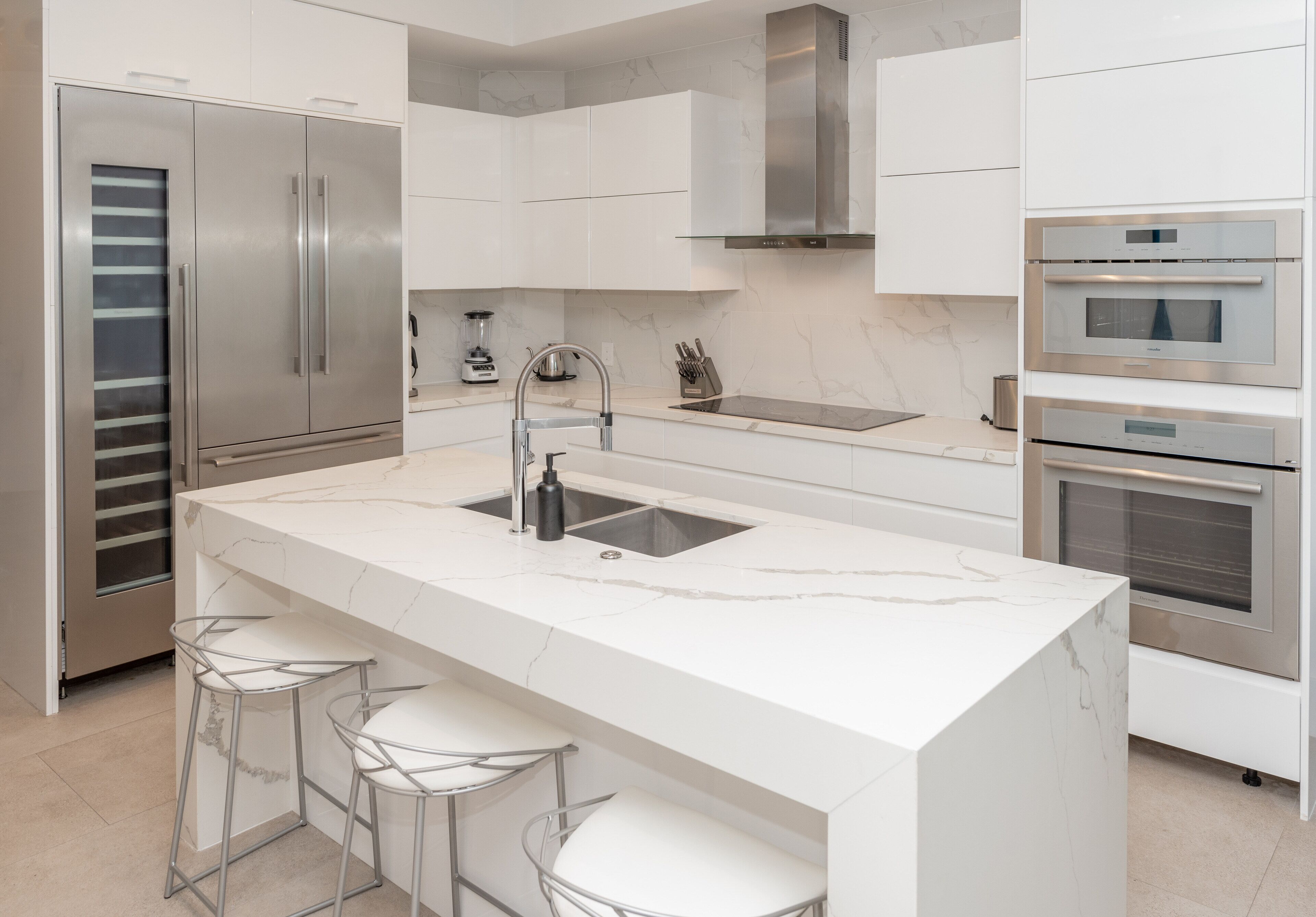 Cozinha moderna com ilha central, eletrodomésticos de aço inoxidável e armários brancos.