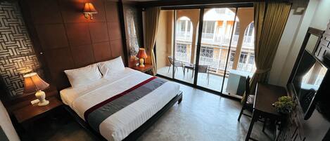Quarto de hotel com uma cama grande, uma escrivaninha com cadeira, televisão e varanda com vista para a cidade.