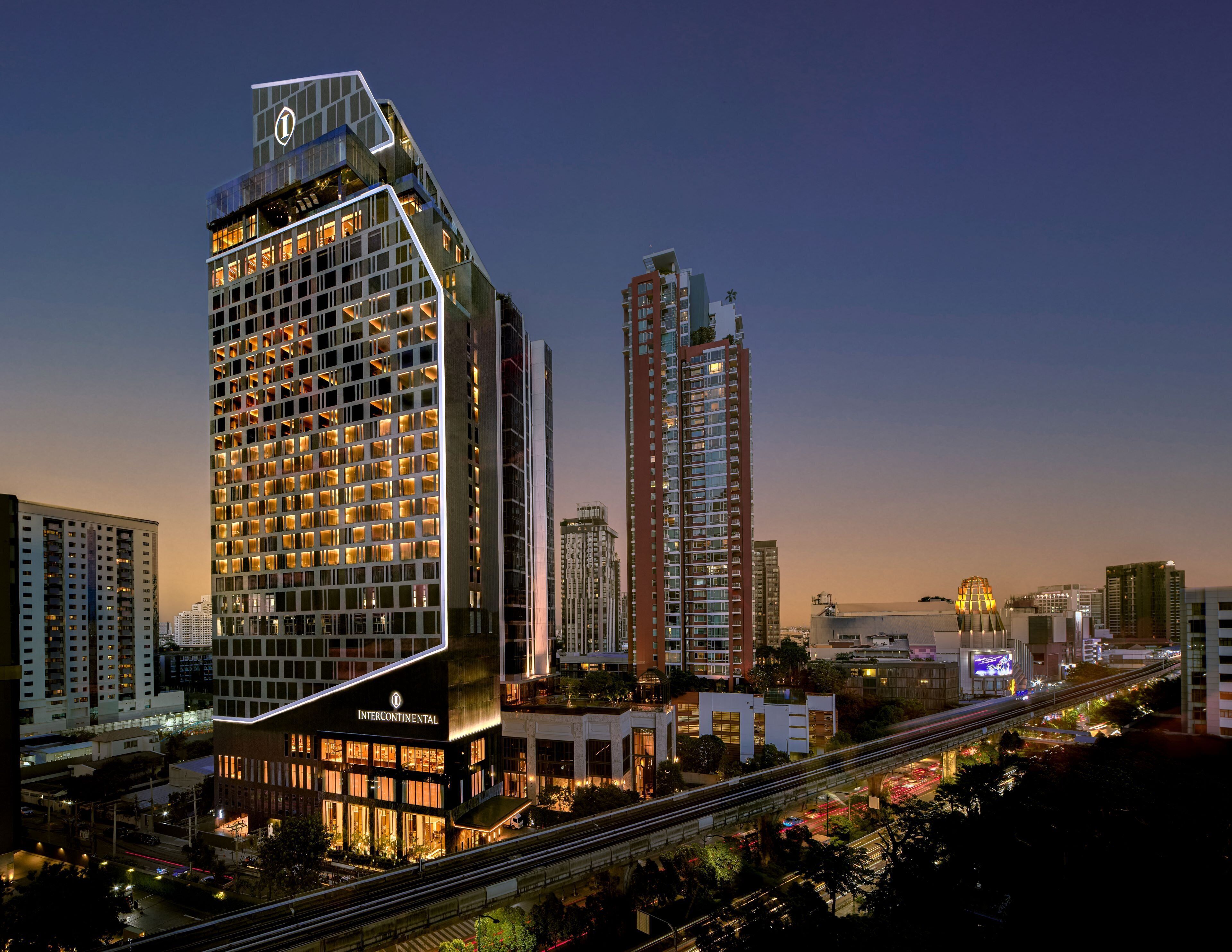 Um hotel imponente com várias andares, um logotipo destacado no topo e fachada bem iluminada.