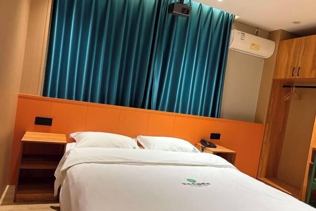Quarto de hotel com cama, mesa de cabeceira, guarda-roupa e janela com cortinas.