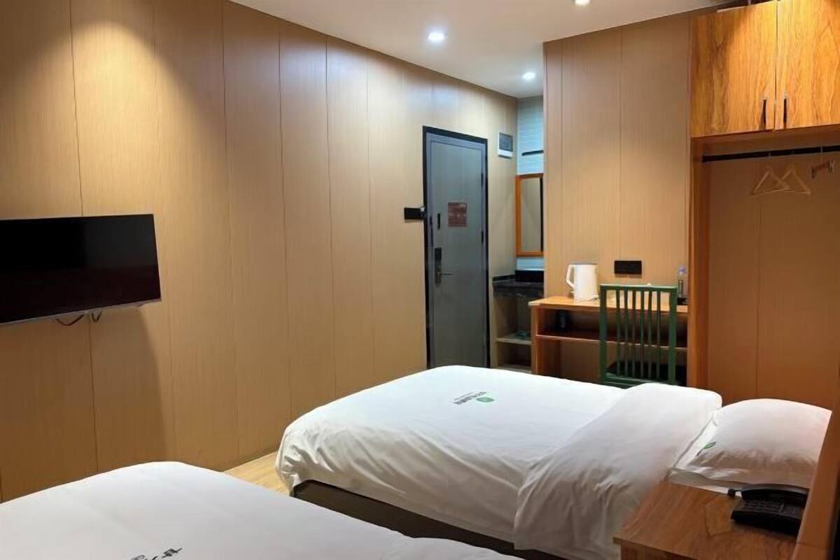 Quarto de hotel com duas camas, uma televisão, um guarda-roupa e uma escrivaninha com cadeira.