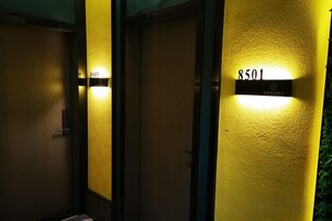Corredor com portas numeradas, parede texturizada e luminária.