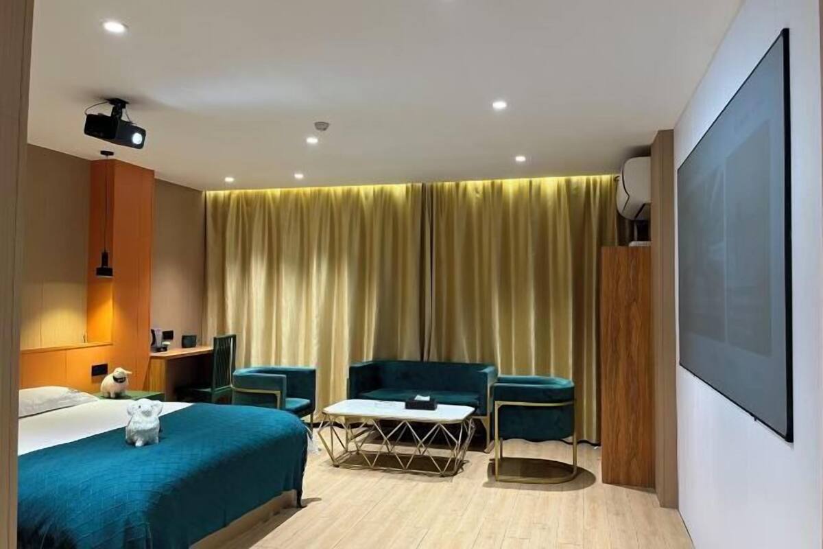 Quarto de hotel com cama, escrivaninha, cadeira, sofá, mesa de centro e projetor.