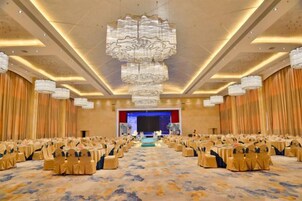 Uma grande sala de conferências com fileiras de cadeiras, palco e lustre.