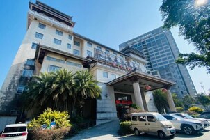 Um hotel com estilo arquitetônico tradicional, apresentando uma entrada imponente com galeria coberta e palmeiras ao primeiro plano.