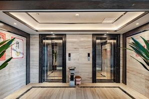 Um elevador moderno com portas de vidro, parede de mármore e teto com iluminação embutida.