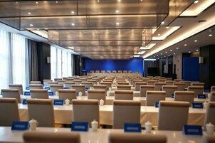 Sala de conferências com mesas e cadeiras dispostas em fileiras, porta-nomes e uma parede com detalhes em azul.