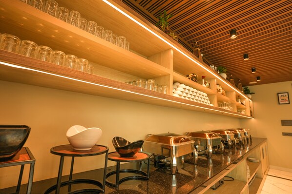 Uma área de bar com prateleiras de copos, um buffet montado e teto de madeira.
