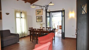 Uma sala de jantar com mesa e cadeiras, um sofá e uma porta que dá para o exterior.