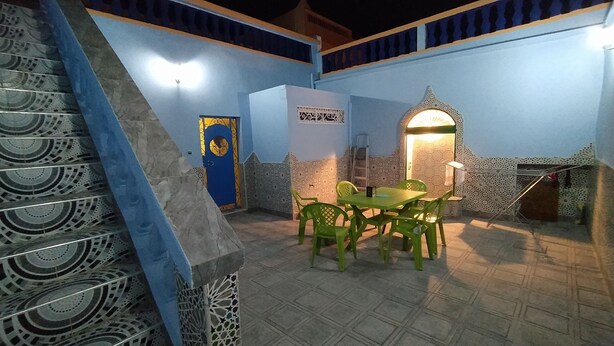 Uma área de refeições ao ar livre com mesa e cadeiras, uma porta azul e desenhos decorativos nas paredes.