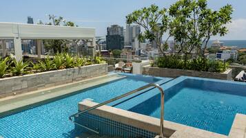 Piscina no terraço com vista para a cidade, cercada por plantas e uma pérgola.