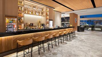 Uma área de bar com um balcão comprido, várias prateleiras de garrafas e uma fileira de banquetas.