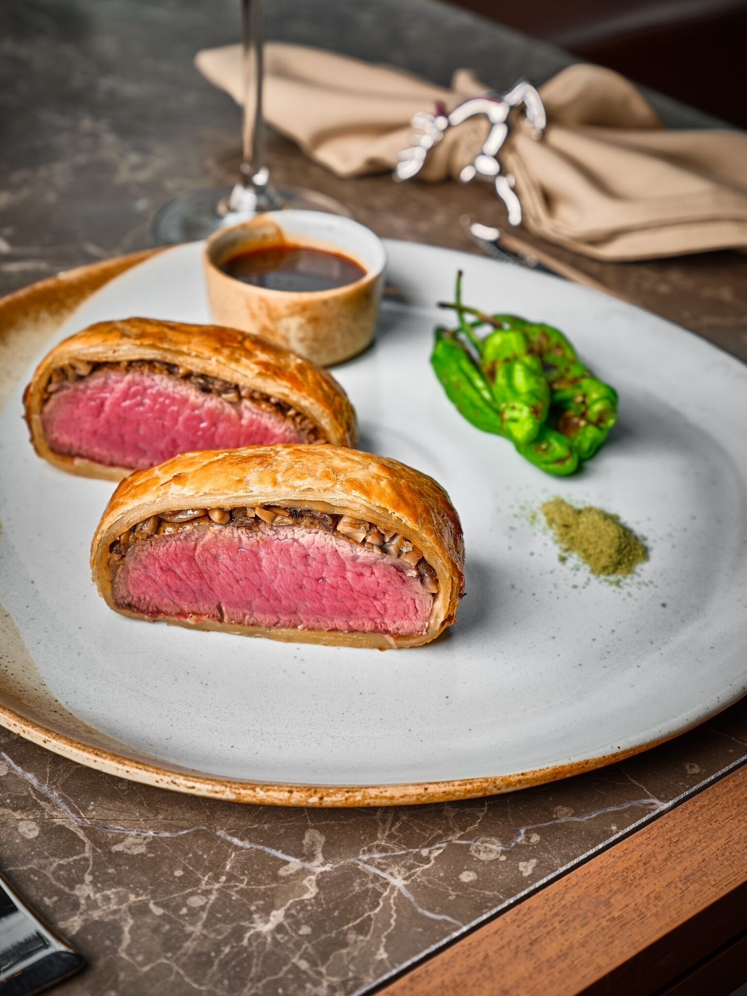 Um prato com carne fatiada, uma pequena tigela de molho e alguns pimentões verdes.