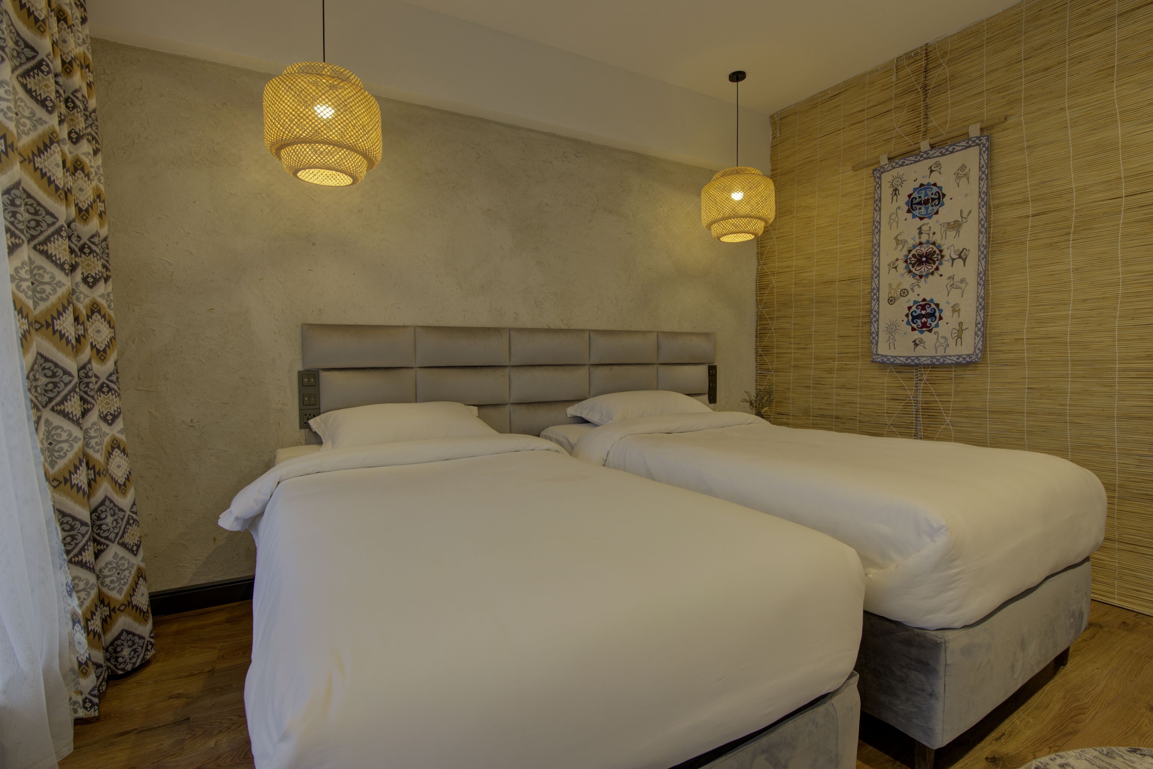 Quarto com duas camas, cabeceira e duas luminárias pendentes.