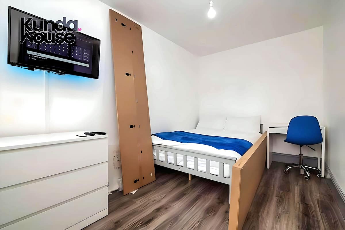 Quarto com cama, escrivaninha, cadeira e televisão exibindo 'Kundla House'.