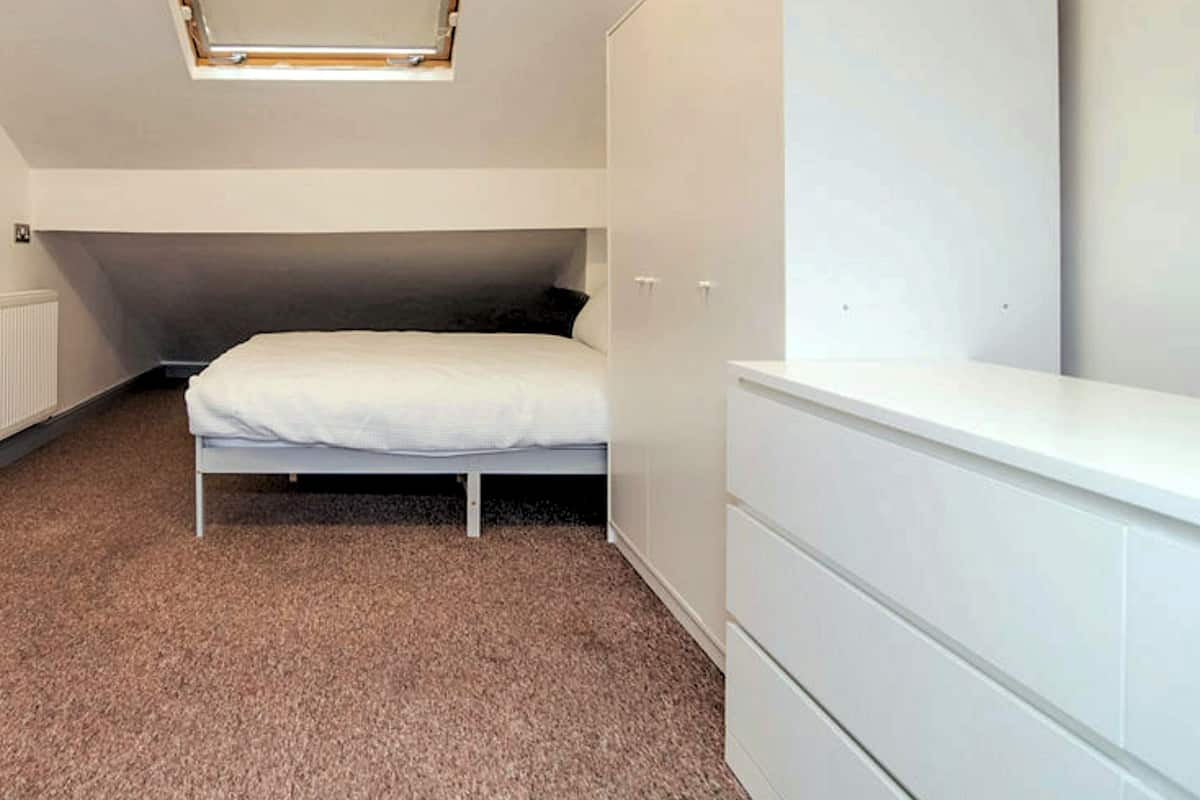 Quarto pequeno e compacto com uma cama beliche, um guarda-roupa branco e teto inclinado com claraboia.