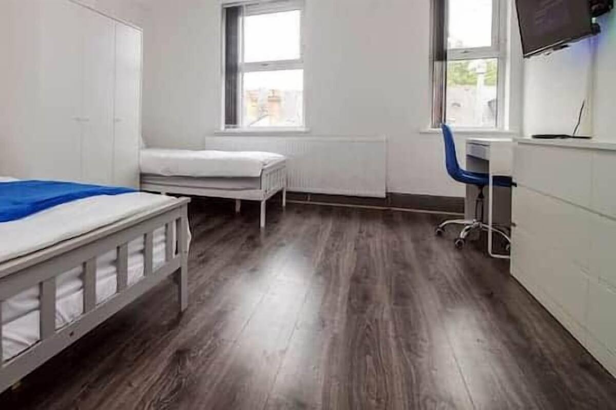 Quarto com cama, escrivaninha, cadeira e janela.