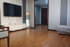 Quarto com televisão de tela plana na parede, penteadeira branca, espelho e cama com colcha estampada.