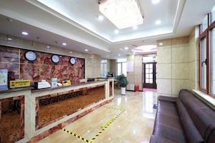 Uma área de recepção de hotel com balcão de mármore, relógios, um sofá e uma janela grande.