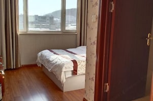 Quarto com cama, piso de madeira, janela e porta.