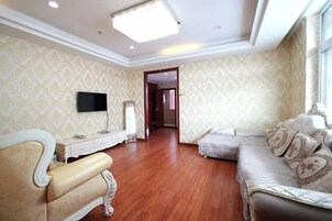 Uma sala de estar ampla, com piso de madeira, um sofá, uma televisão e um espelho sobre um aparador.