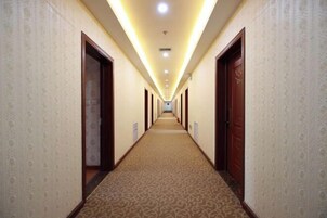Corredor de hotel com pisos carpetados, portas de madeira e papel de parede estampado.
