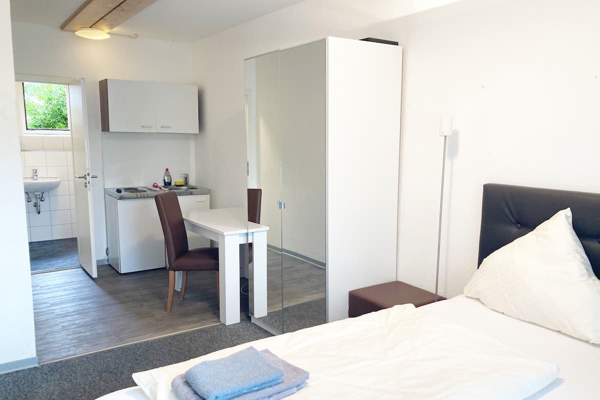 Quarto de hotel moderno com cama, escrivaninha e cozinha compacta.