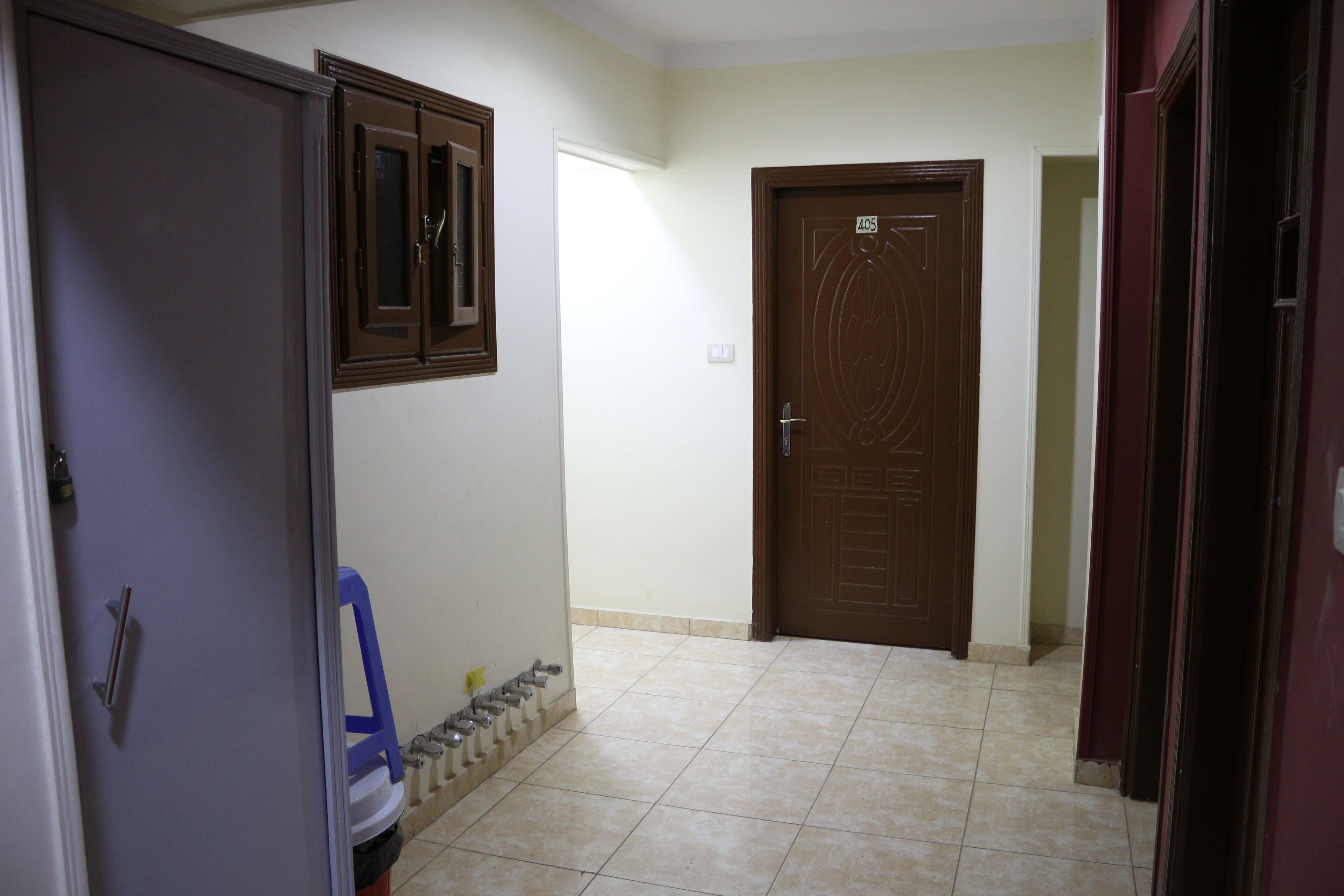Um corredor com uma porta fechada, uma cadeira azul e um sanitário.