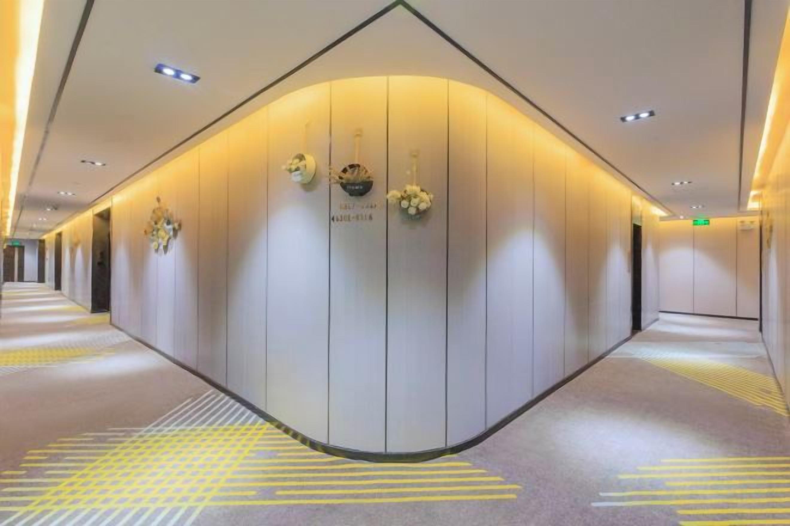 Corredor de hotel com parede curva, balcão de recepção e piso coberto por carpete.