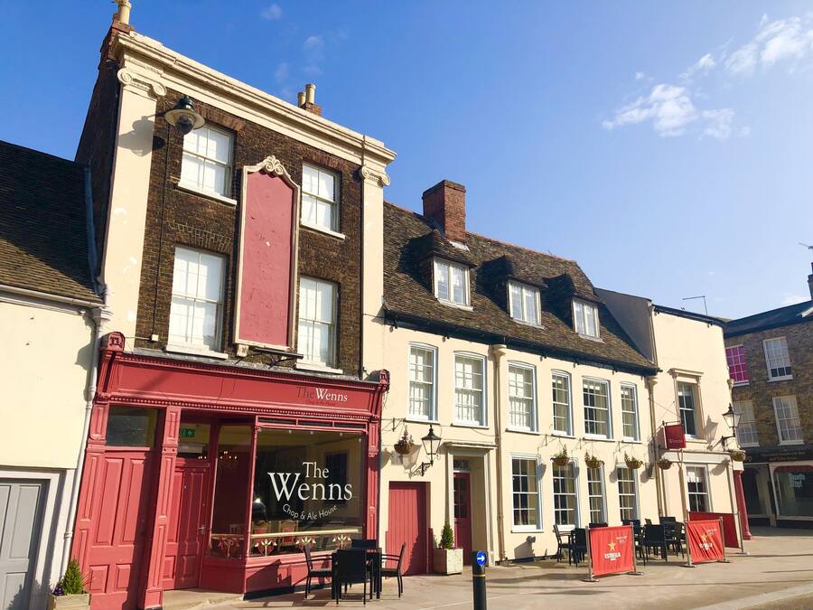 Um pub tradicional chamado 'The Wenns', com fachada vermelha, várias janelas e área de estar ao ar livre.