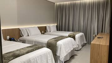 Quarto de hotel com duas camas, uma secretária de madeira, um telefone e uma cortina.