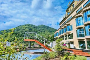 Hotel com piscina, uma ponte e montanhas ao fundo.