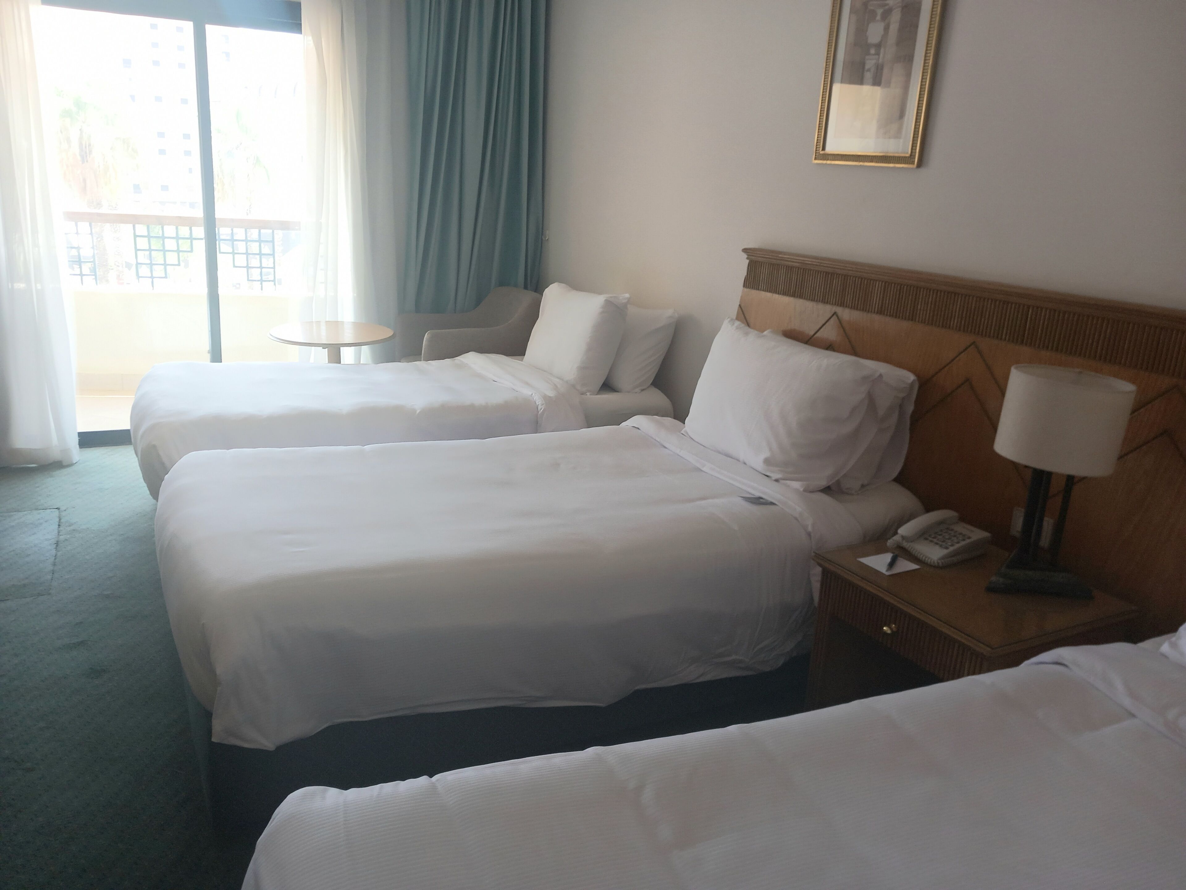 Quarto de hotel com duas camas, uma mesa pequena, uma luminária e um telefone na mesinha de cabeceira.