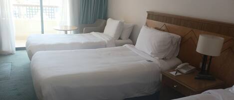 Quarto de hotel com duas camas, uma mesa pequena, uma luminária e um telefone na mesinha de cabeceira.