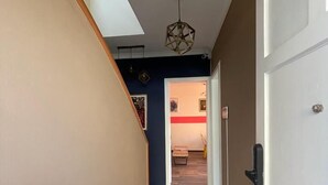 Um corredor com escada de madeira, luminária no teto e porta com puxador.