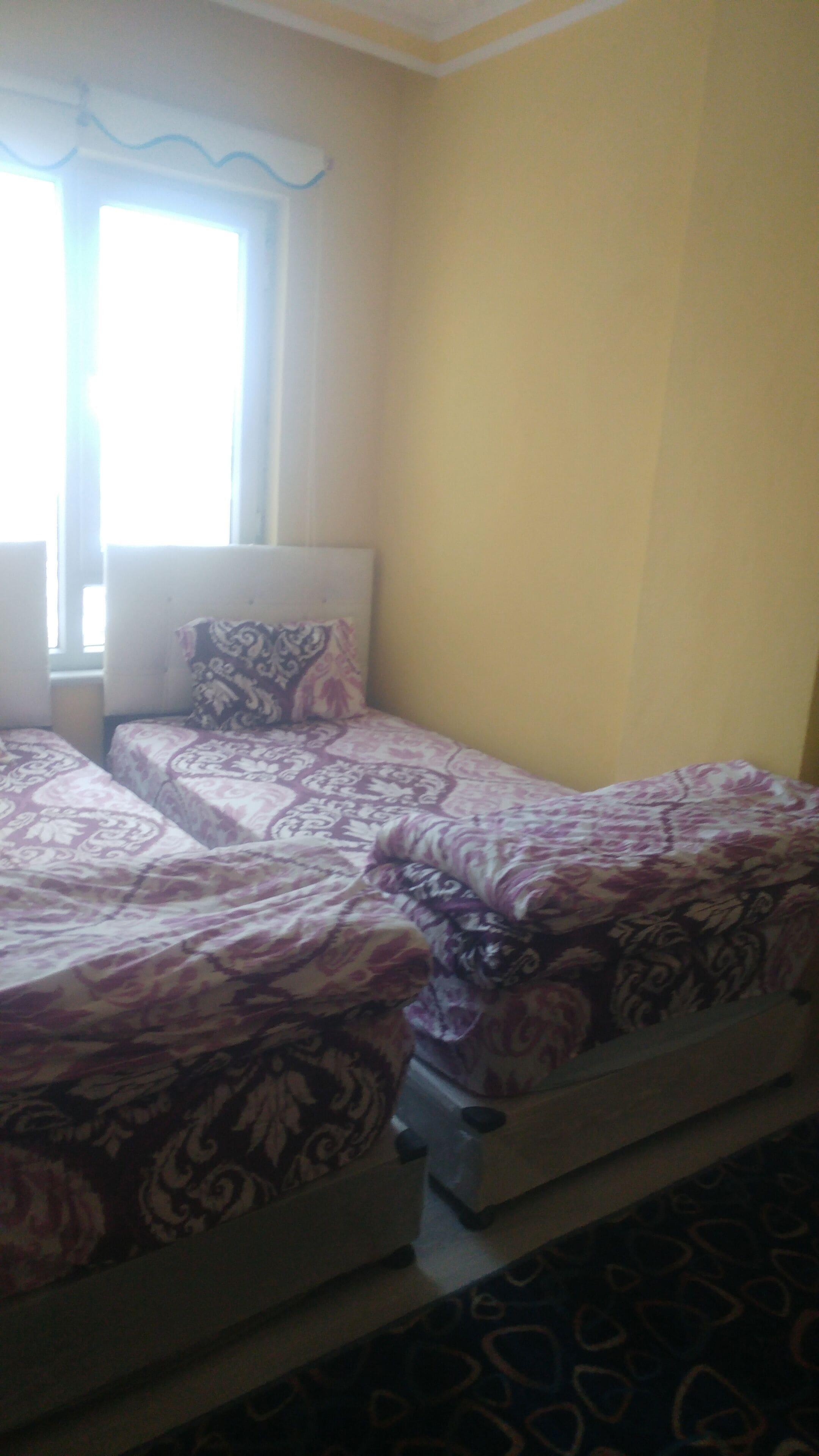 Quarto com duas camas, uma janela e parede amarela.