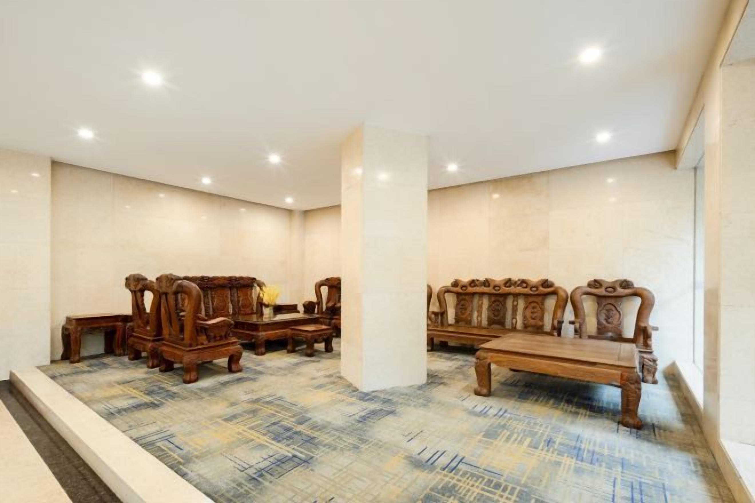 Um hall de hotel com uma coluna central, área de estar com mobiliário de madeira e carpete estampado.
