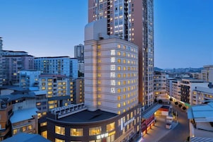 Um hotel moderno com vários andares, entrada destacada em esquina e fachada bem iluminada.