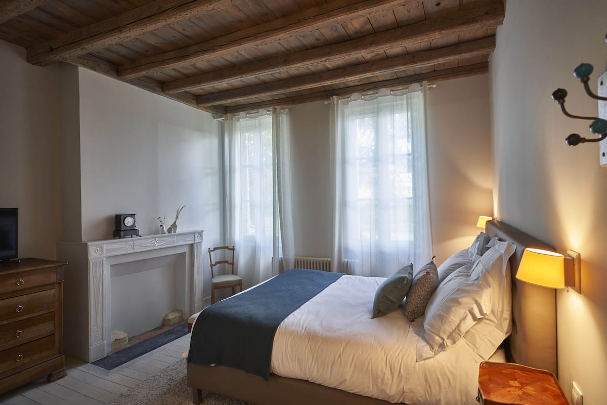 Um quarto com uma cama, cômoda, lareira e mesa de cabeceira.